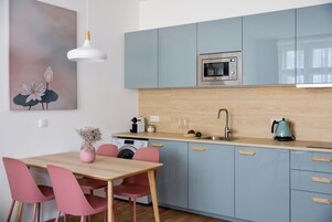 Uma cozinha moderna com armários azul-claros, bancada de madeira, micro-ondas embutido, pia e cafeteira. Há uma mesa de jantar com cadeiras cor-de-rosa e um vaso de flores.
