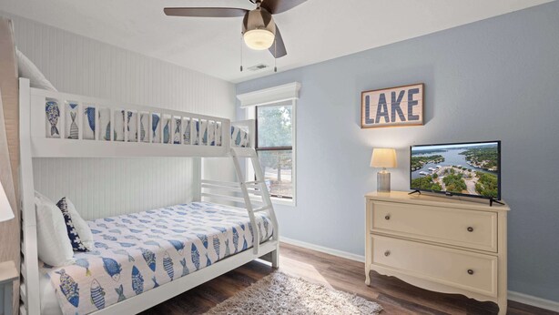 Quarto com beliches, cômoda, televisão e janela com vista para um lago.