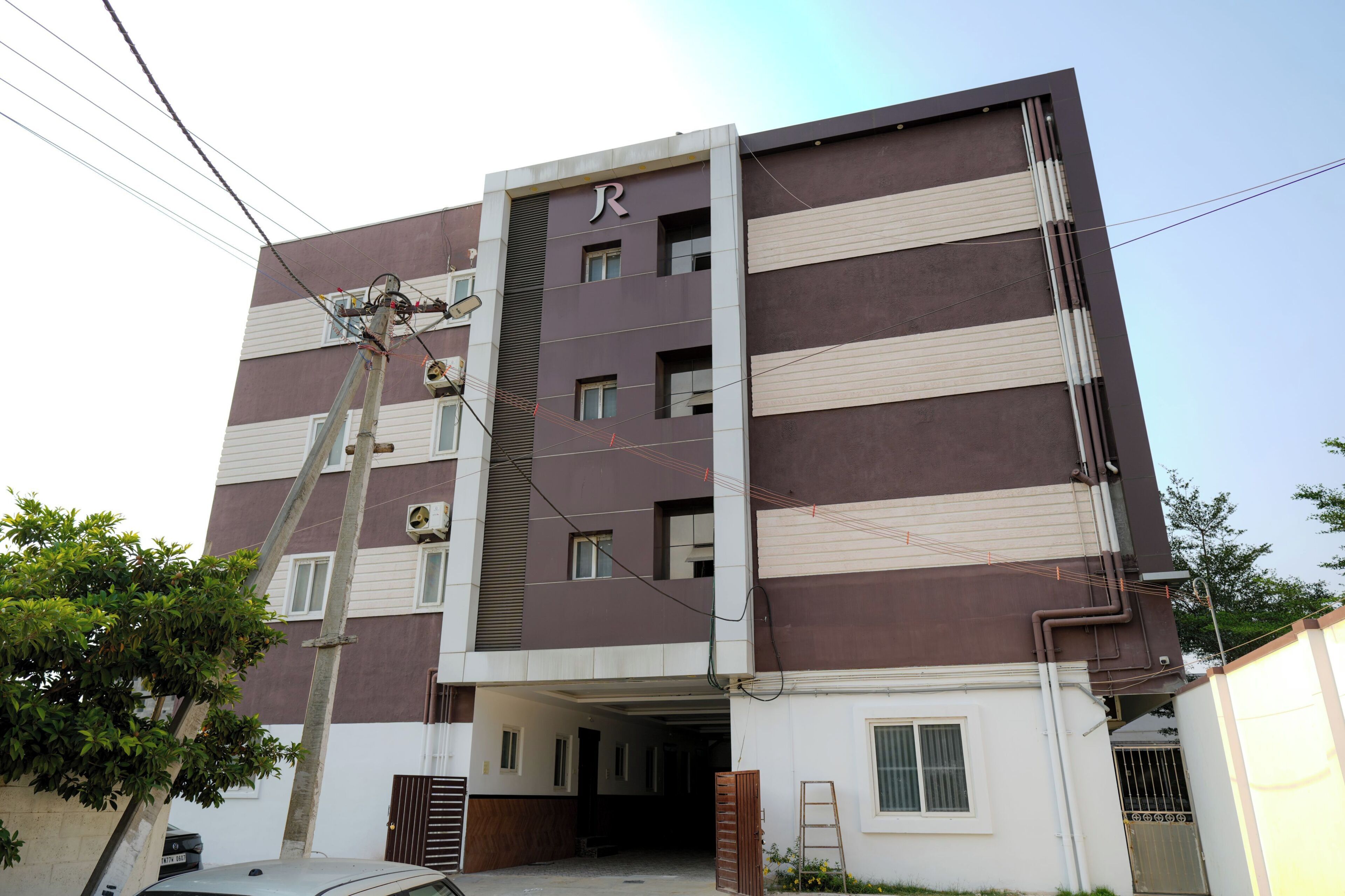 Edifício residencial com vários andares, um eixo de elevador central, entrada de garagem visível e uma árvore em primeiro plano.