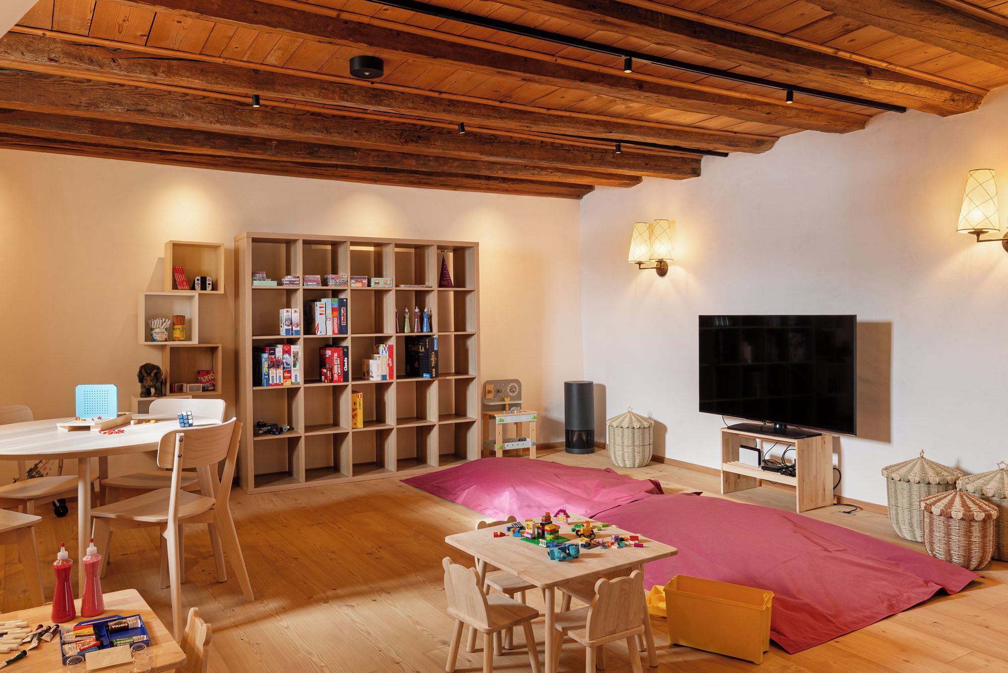 Uma sala de estar aconchegante com teto de madeira, estante de livros, televisão e um espaço para brincar com brinquedos e um tapete rosa.