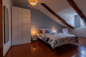 Quarto com cama, mesas de cabeceira, guarda-roupa e teto inclinado com vigas aparentes.