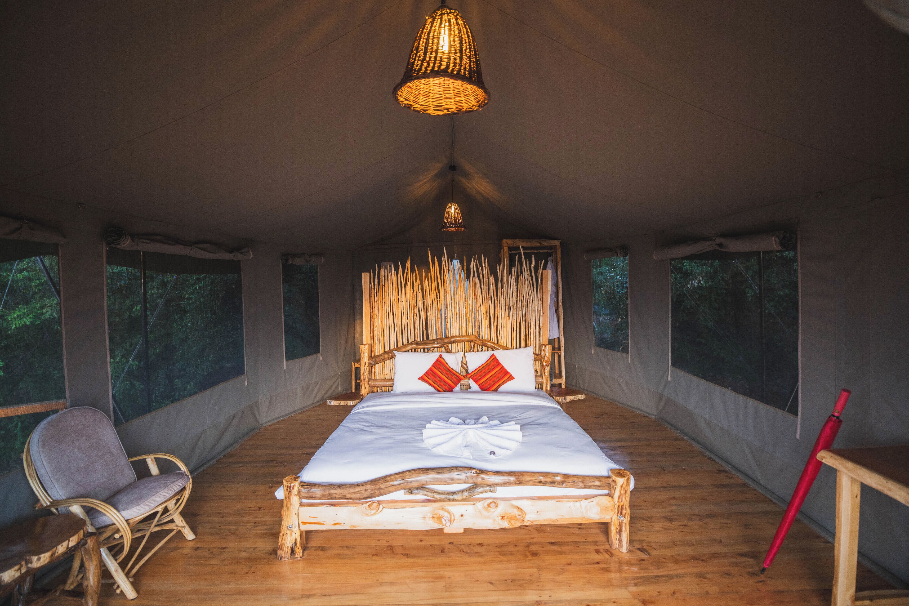 Quarto tipo tenda com cama, móveis de madeira e luminária pendente.