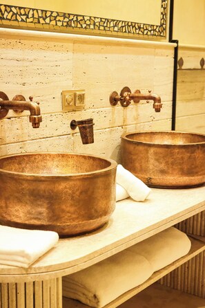 Casa de banho com duas pias de cobre, um espelho e uma parede revestida a azulejos.