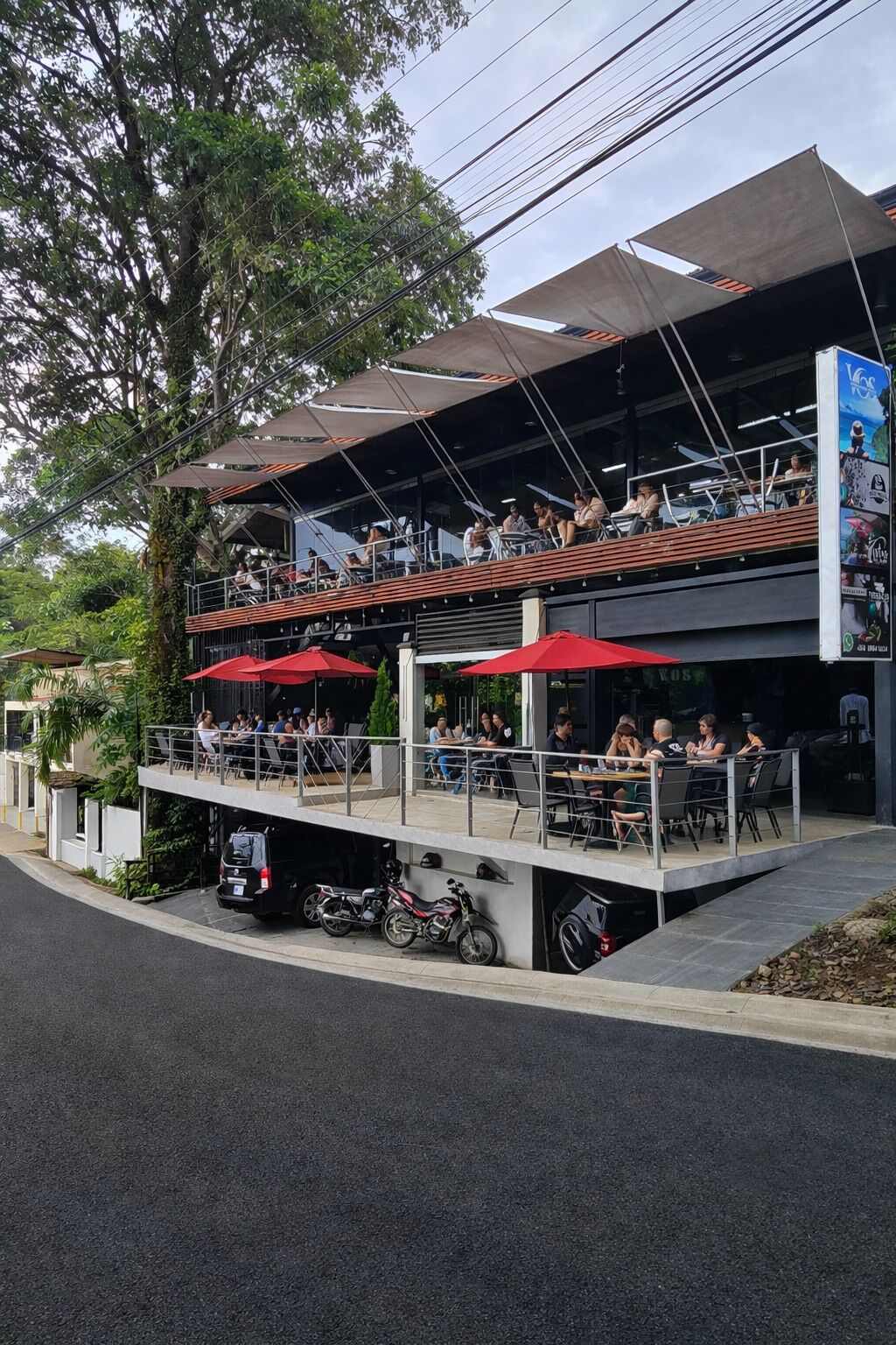 Um restaurante ao ar livre com várias áreas de refeição, assentos cobertos e vista para a rua.