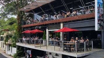 Um restaurante ao ar livre com várias áreas de refeição, assentos cobertos e vista para a rua.
