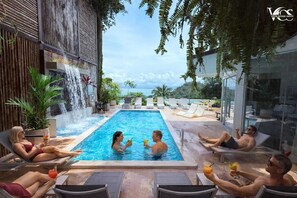 Uma área de piscina com cascata, espreguiçadeiras e vista para o oceano.