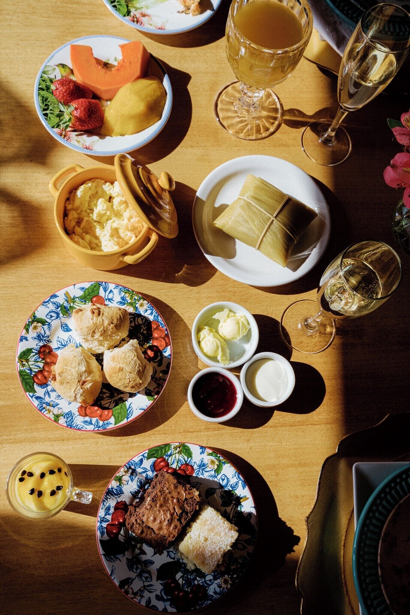 Uma mesa com diversos pratos, incluindo uma tigela de frutas, um prato de scones e uma taça de vinho.