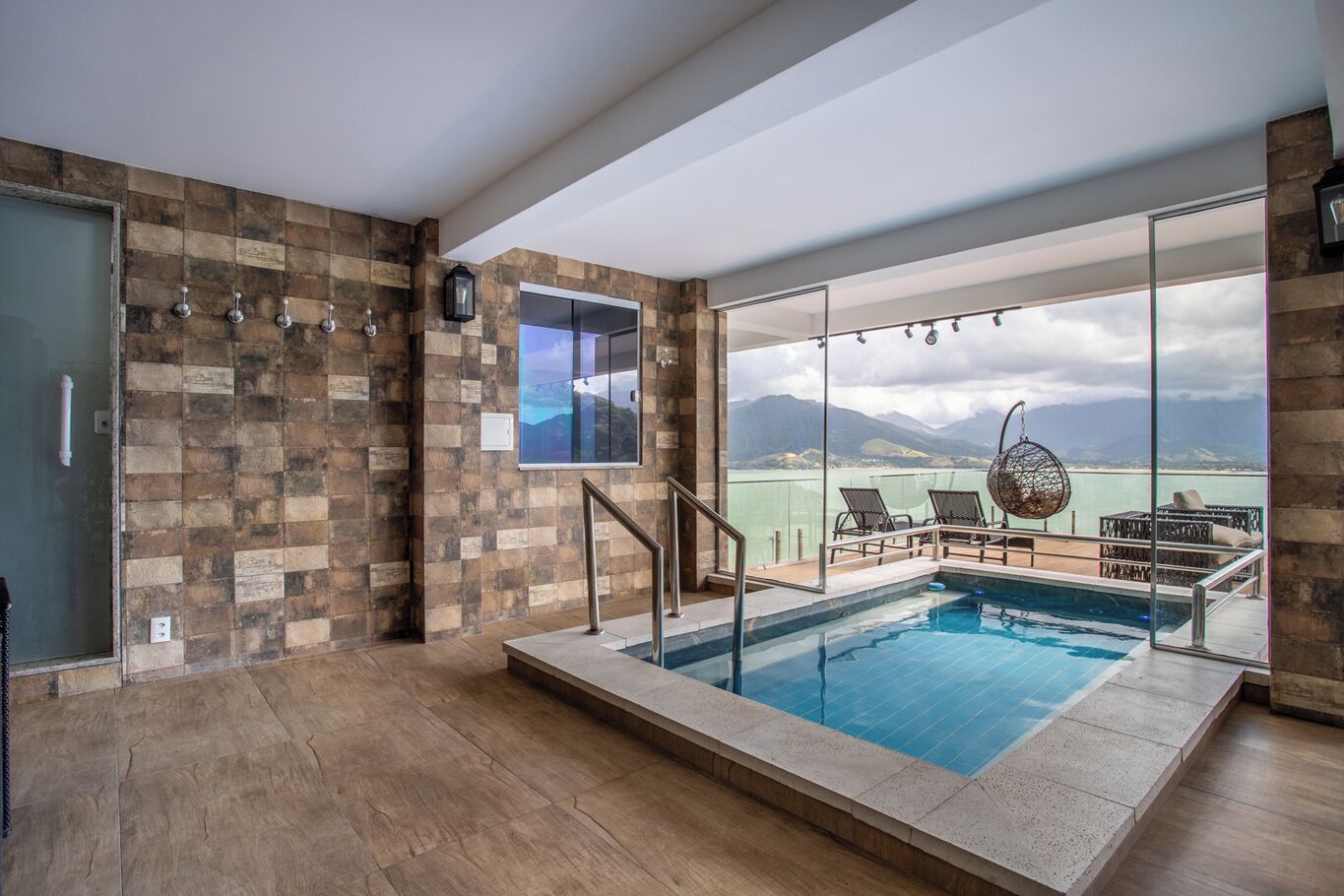 Área interna de piscina moderna com vista para montanhas e um corpo d'água.