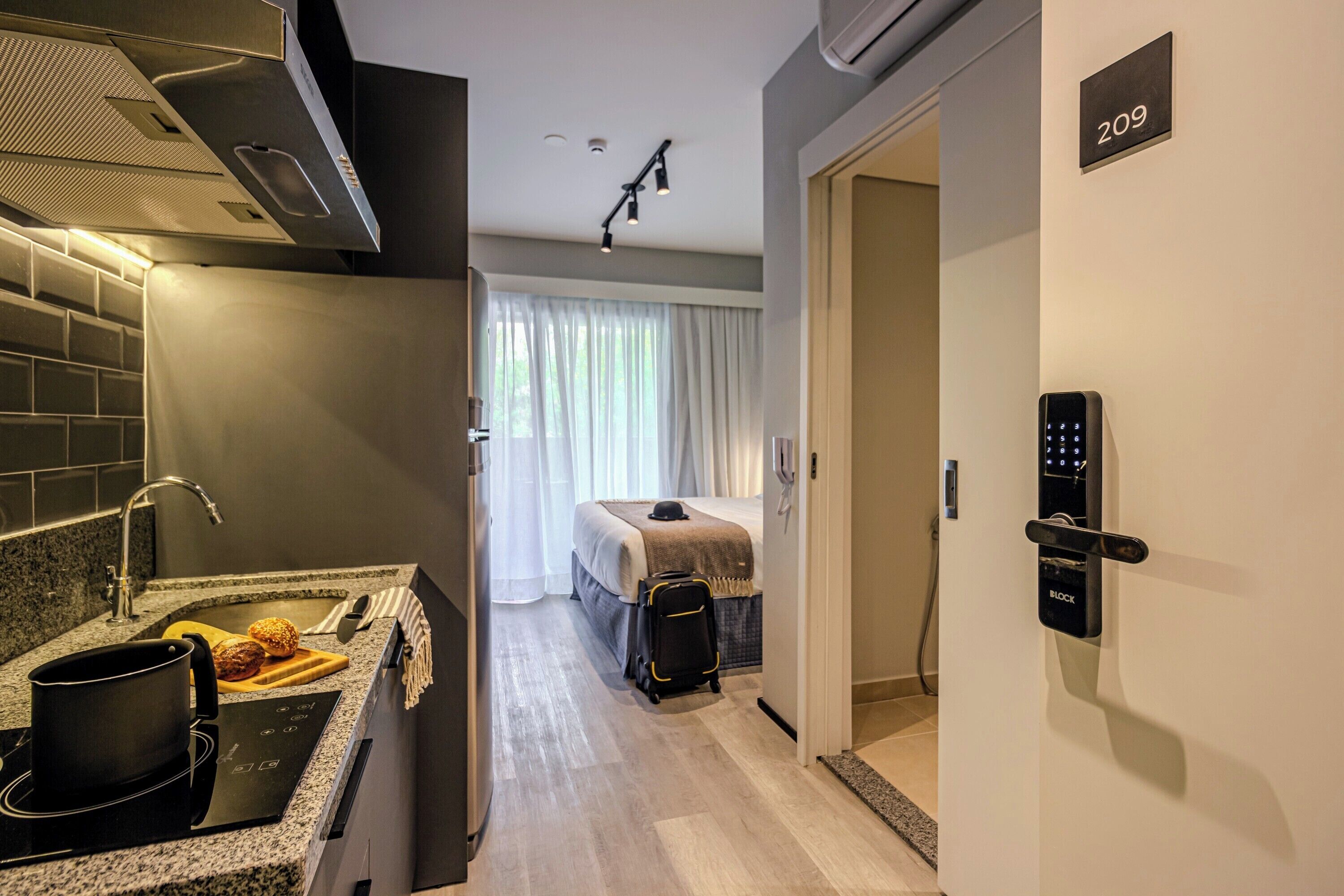 Quarto de hotel moderno com cozinha compacta, cama com vista e fechadura digital.