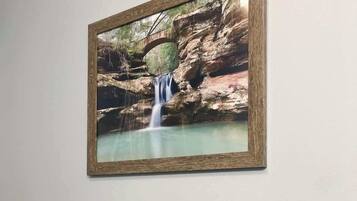 Um banheiro com uma imagem emoldurada de uma cachoeira, um porta-toalhas com uma toalha e um rodapé branco.