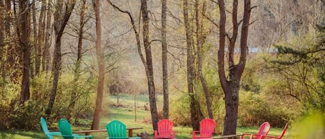 Uma área arborizada com uma fogueira e várias cadeiras Adirondack em verde e vermelho.