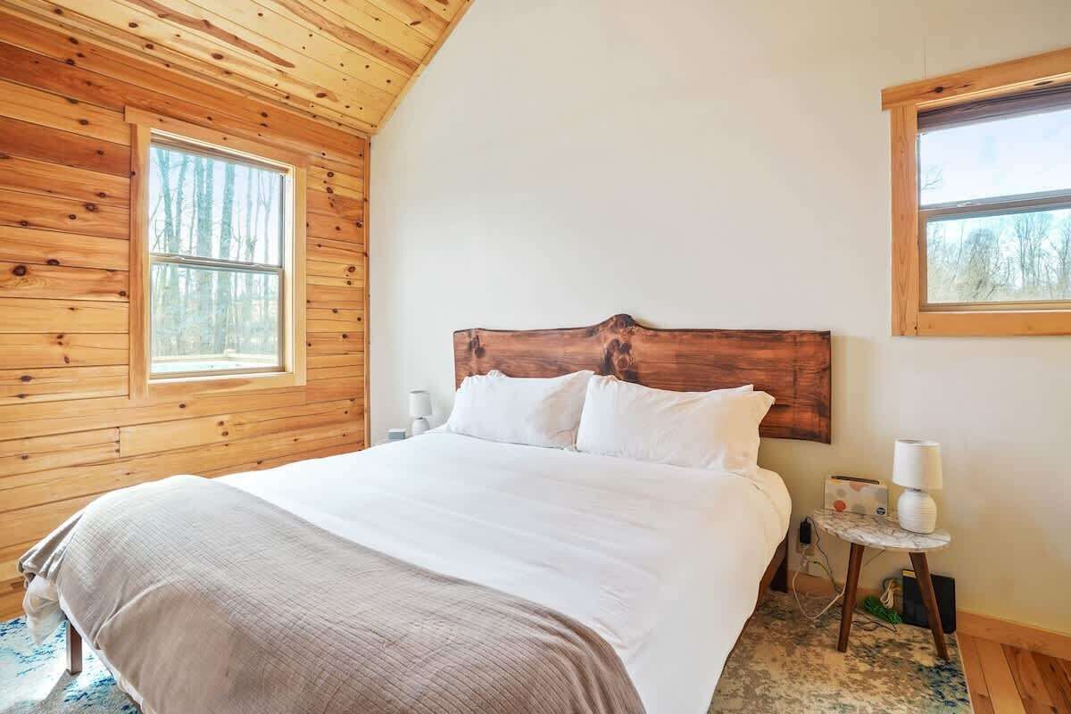 Um quarto com painéis de madeira, uma cama grande, duas janelas e uma pequena mesa de cabeceira com abajur.