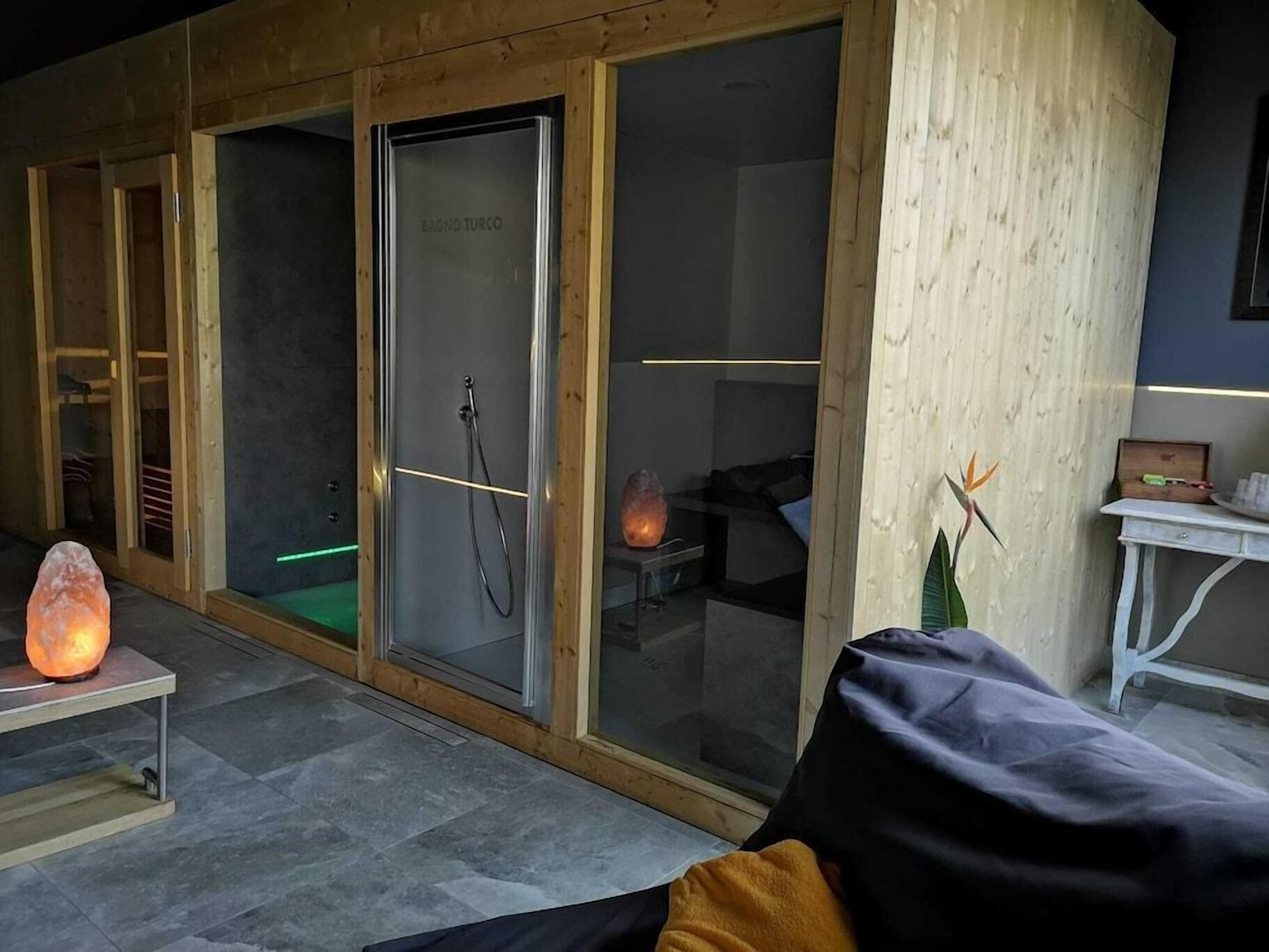 Um espaço de spa com sauna, chuveiro em cabine de vidro e mesa para massagem.