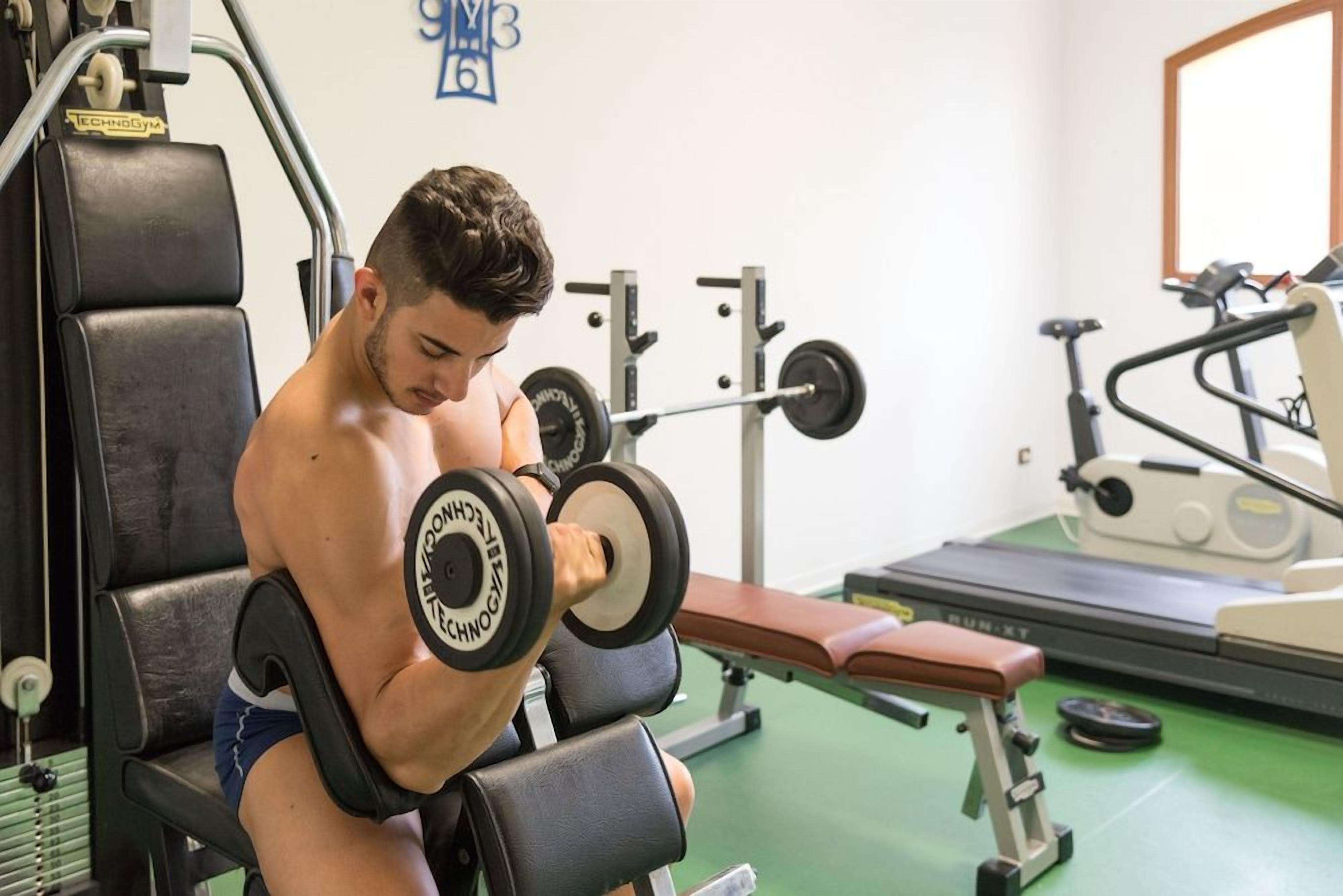 Academia com equipamentos de ginástica, incluindo um banco e halteres.