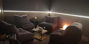Um quarto com iluminação suave e design moderno, com um sofá, uma mesa com bebidas e uma luminária fixada na parede.