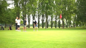 Um campo de golfe com uma bandeira vermelha, árvores e pessoas em pé na relva.