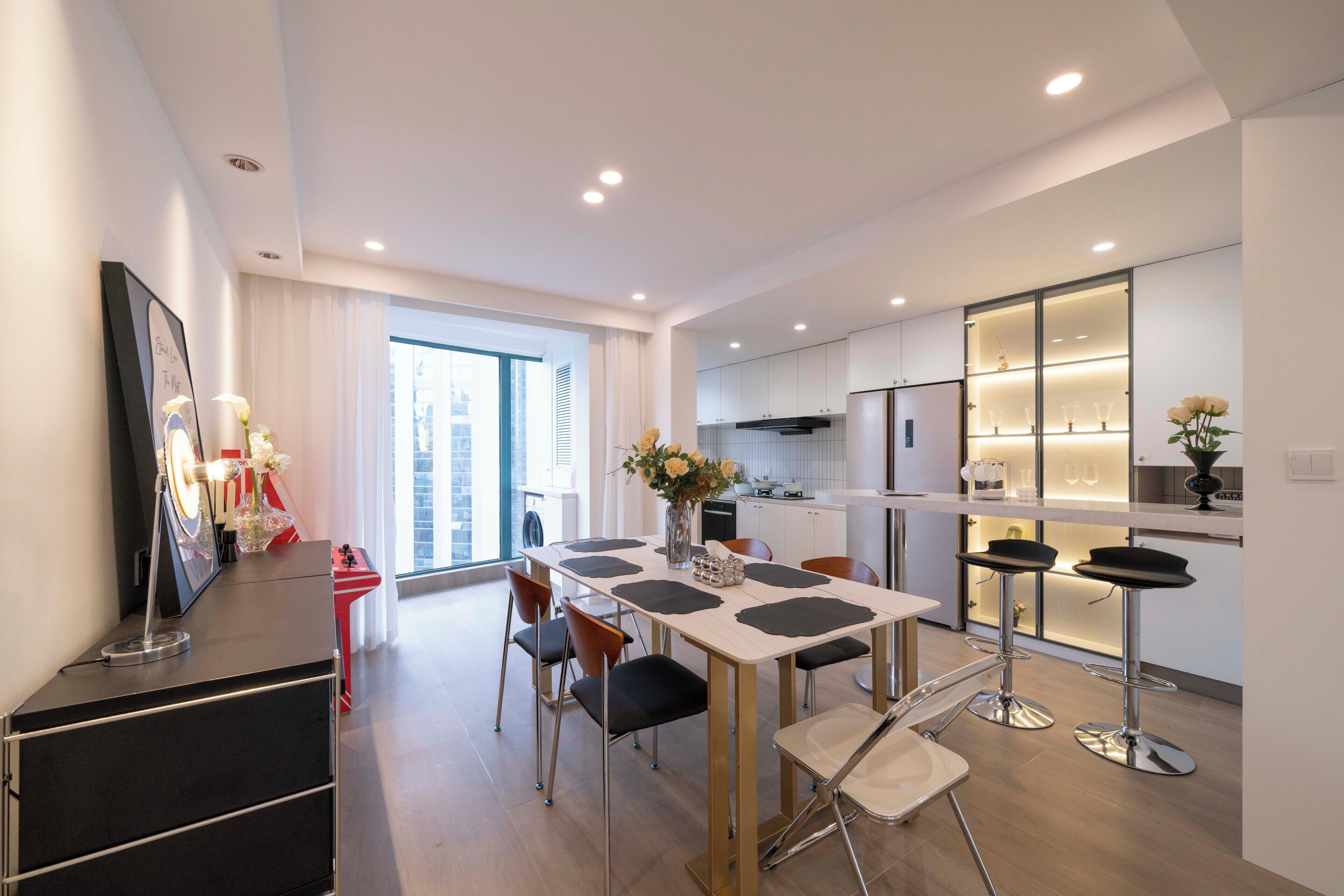 Cozinha moderna com armários brancos, área de refeições com mesa e cadeiras, e um balcão com banquetas.