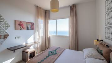 Quarto de hotel com cama, mesa de cabeceira, janela com cortinas, luminária na parede e um quadro.