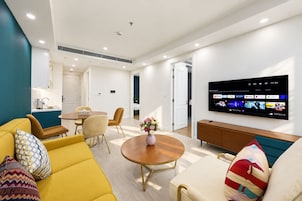 Uma sala de estar moderna com um sofá amarelo, uma mesa de centro redonda e uma televisão de tela plana fixada na parede.