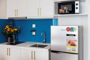 Cozinha com armários brancos, painel de parede azul, pia de aço inoxidável, micro-ondas e geladeira com o logotipo Panasonic.