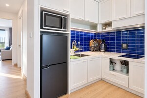 Cozinha moderna com armários brancos, geladeira preta, micro-ondas e painel de azulejos azuis.