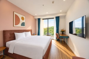 Quarto de hotel com uma cama grande, uma escrivaninha, uma cadeira e uma televisão.