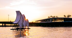 Um edifício moderno com uma estrutura singular em forma de vela, diante de um pôr do sol.