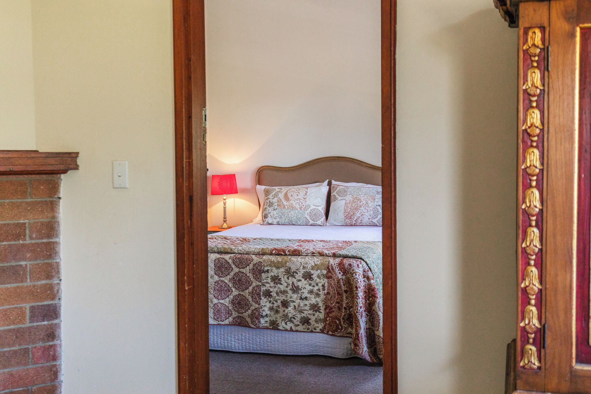 Quarto com cama, mesa de cabeceira, abajur e moldura de porta de madeira.