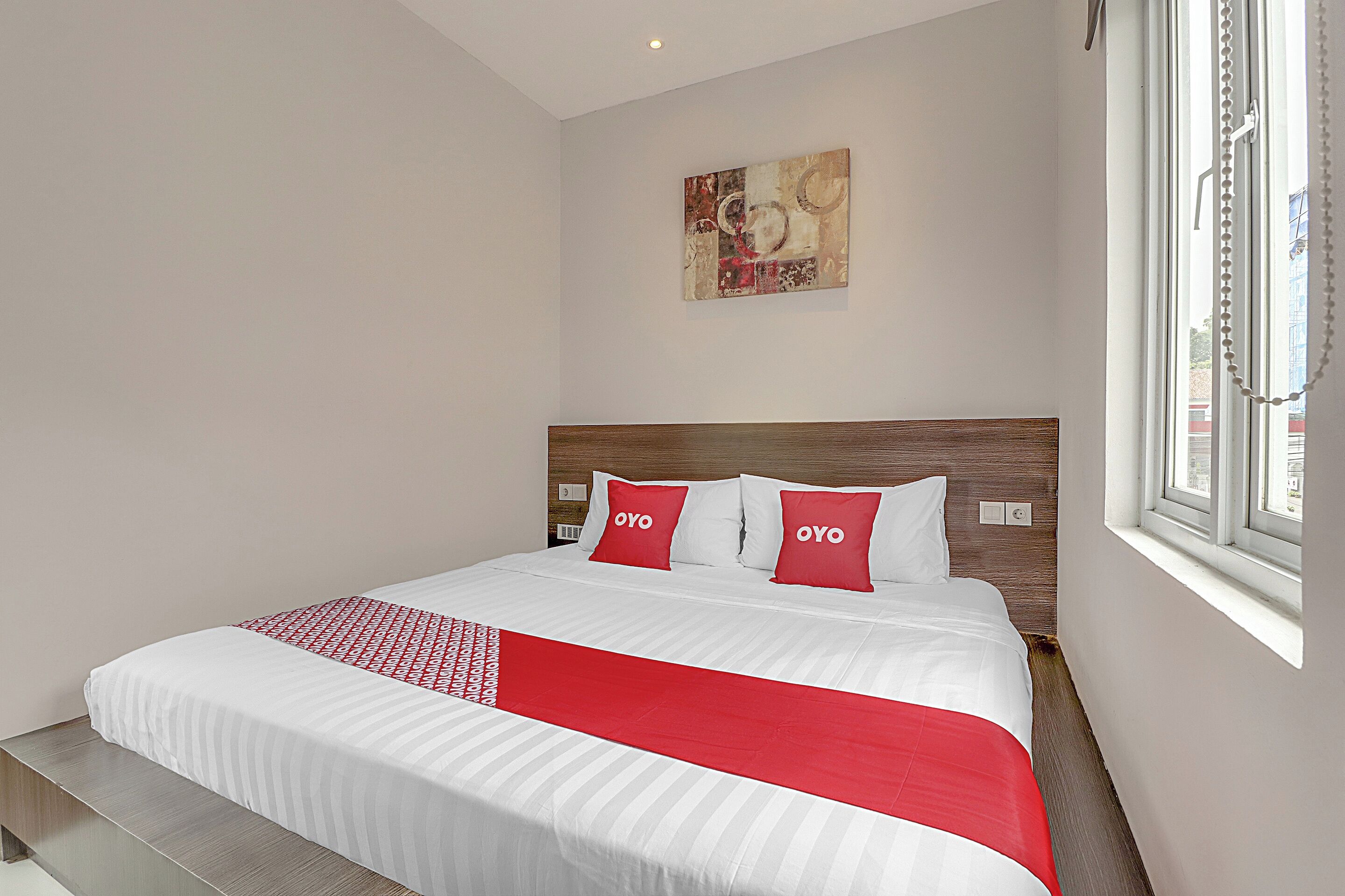 Quarto de hotel com uma cama grande, colcha vermelha e branca e um quadro na parede.