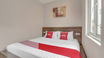 Quarto de hotel com uma cama grande, colcha vermelha e branca e um quadro na parede.