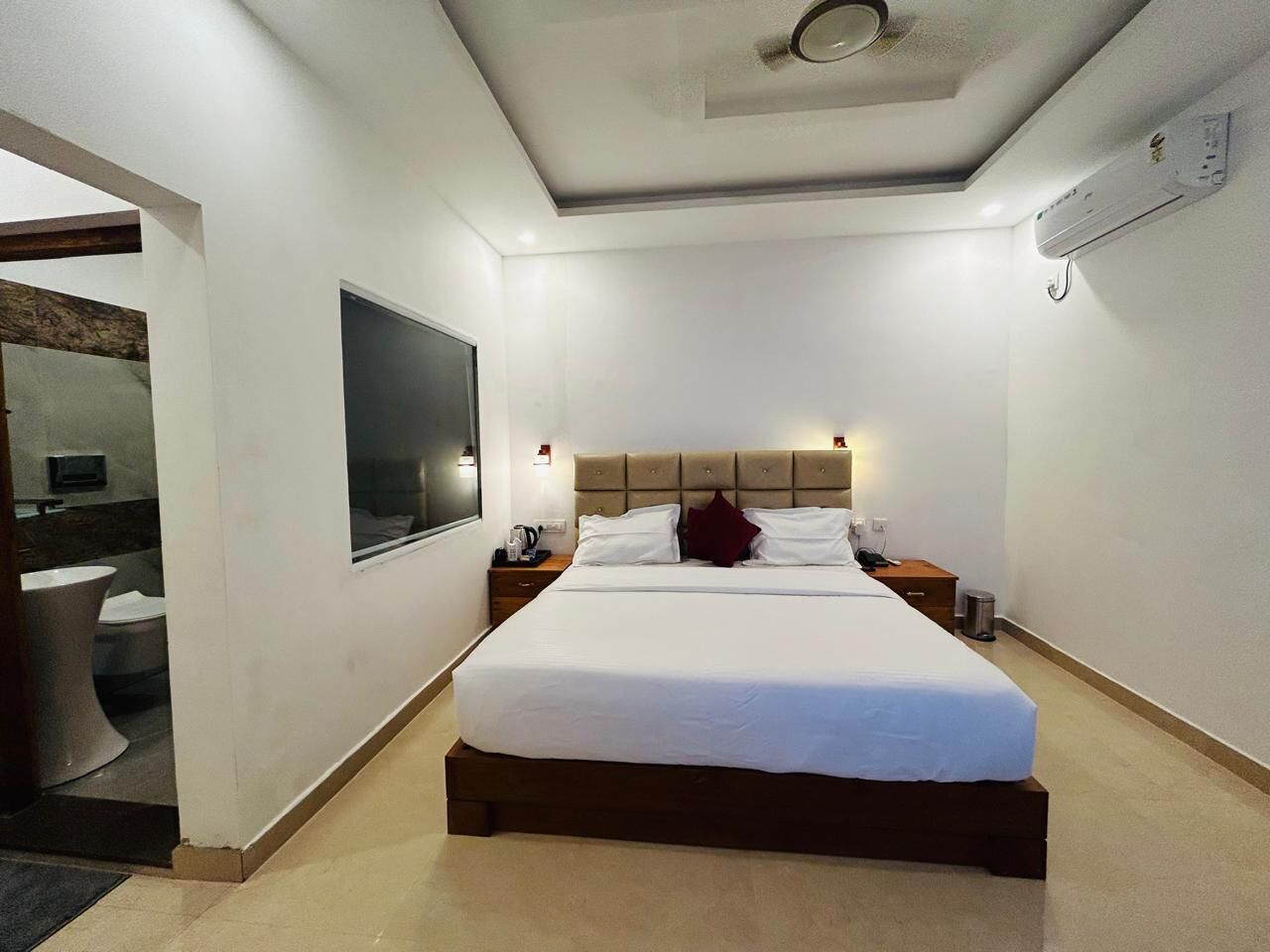 Quarto de hotel moderno com uma cama grande, mesas de cabeceira, uma televisão de tela plana e um banheiro visível através de uma porta aberta.