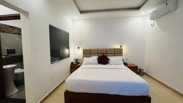 Quarto de hotel moderno com uma cama grande, mesas de cabeceira, uma televisão de tela plana e um banheiro visível através de uma porta aberta.