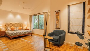 Um quarto com cama, uma cadeira, janela com cortinas, ventilador de teto e uma obra de arte na parede.