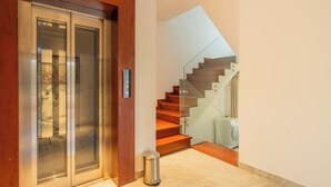 Um interior moderno com elevador de vidro, escada de madeira e piso de mármore.