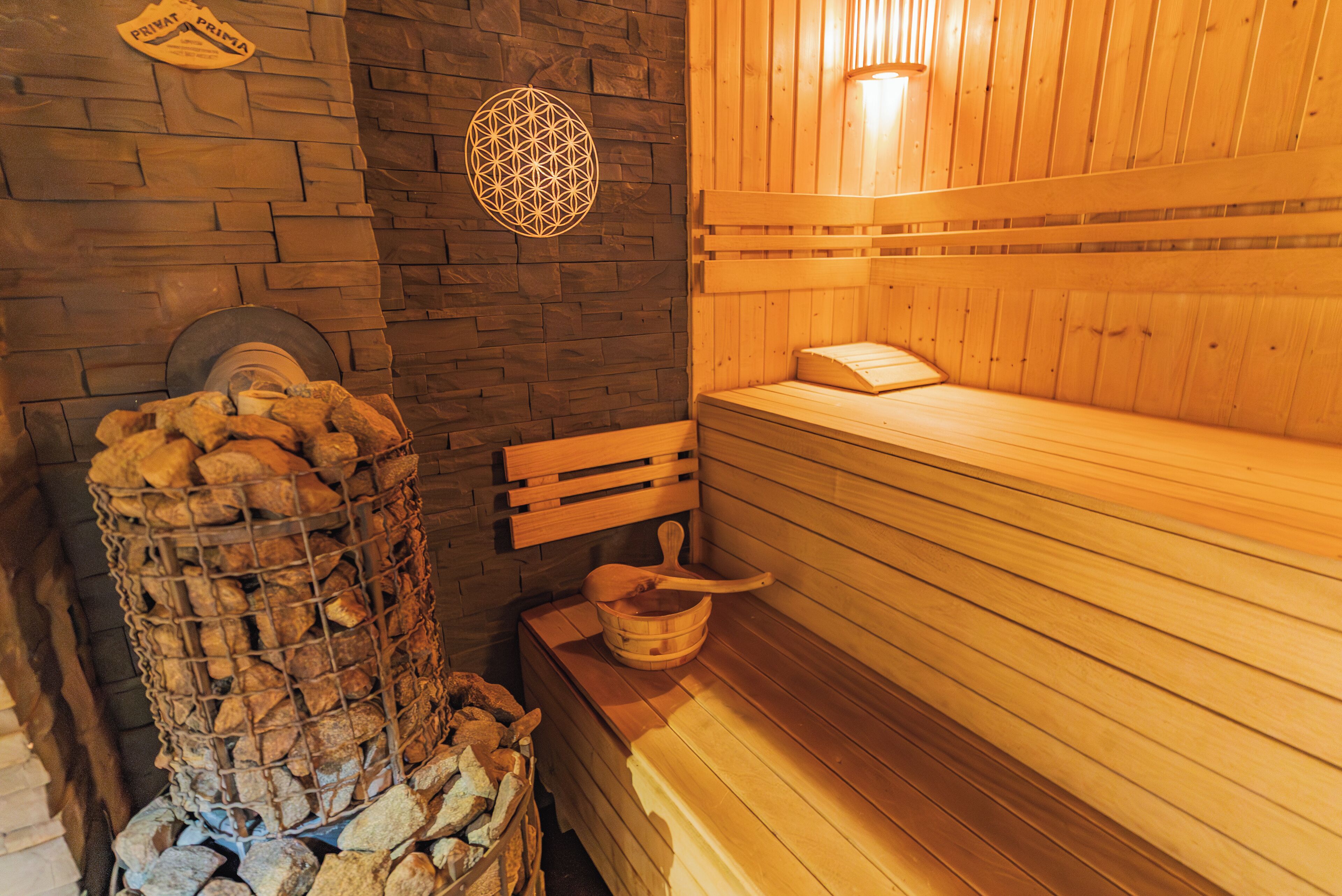 Uma sauna com bancos de madeira, parede de pedra e um recipiente de metal com pedras.
