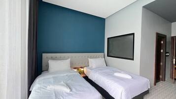 Quarto de hotel com duas camas, uma janela grande e uma porta que dá para outro quarto.