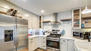 Cozinha moderna com eletrodomésticos de aço inoxidável, armários brancos e piso de madeira.