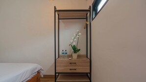 Quarto com cama, mesa de cabeceira de madeira com uma planta e um criado-mudo.