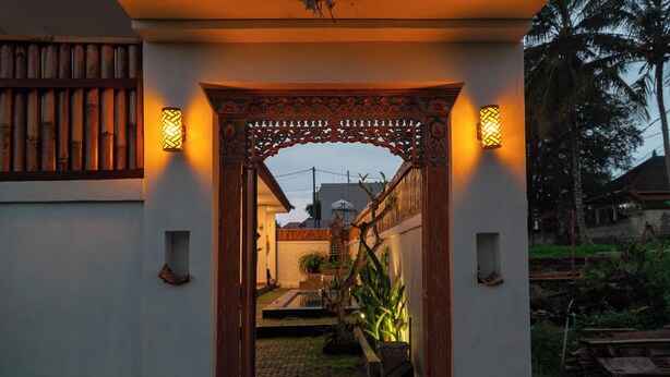 Uma entrada com um arco decorativo, um caminho que leva a um edifício e uma pequena área de jardim com plantas.