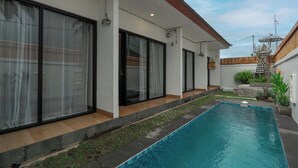 Uma casa moderna com piscina, grandes portas de vidro deslizantes e um pequeno jardim.