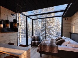 Interior moderno com cama, área de estar e uma grande janela com vista para uma floresta coberta de neve.