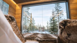 Interior acolhedor de uma cabana com uma grande janela com vista para uma floresta coberta de neve.