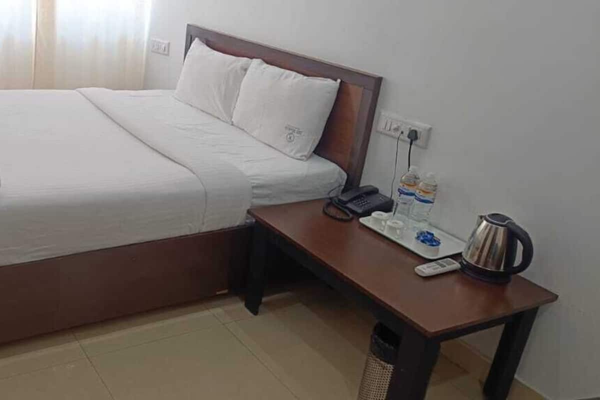 Uma cama bem arrumada com edredom branco e travesseiros, mesa de cabeceira com telefone, chaleira e garrafa de água.
