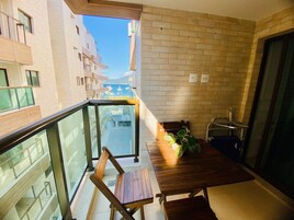 Varanda com mesa e cadeiras de madeira, um vaso de planta e vista para edifícios e barcos.