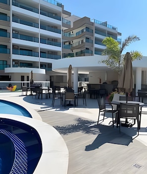 Uma área de piscina no terraço com mobiliário externo e um edifício moderno ao fundo.