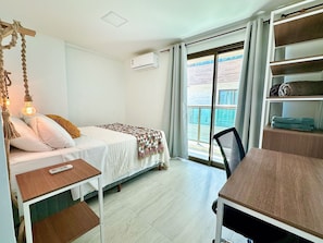Um quarto com uma cama, uma escrivaninha, uma cadeira, luminária pendente, janela com cortinas e ar-condicionado fixado na parede.