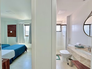 Quarto de hotel com cama, banheiro com vaso sanitário e pia, e chuveiro.