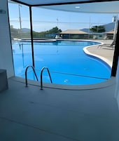Uma piscina interior moderna com paredes de vidro transparente, design curvo e escada de metal.