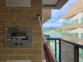 Uma varanda com forno de aço inoxidável, vista para uma paisagem montanhosa e um edifício com amplas janelas.
