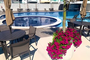 Área da piscina com espreguiçadeiras, ofurô e um vaso de flores.